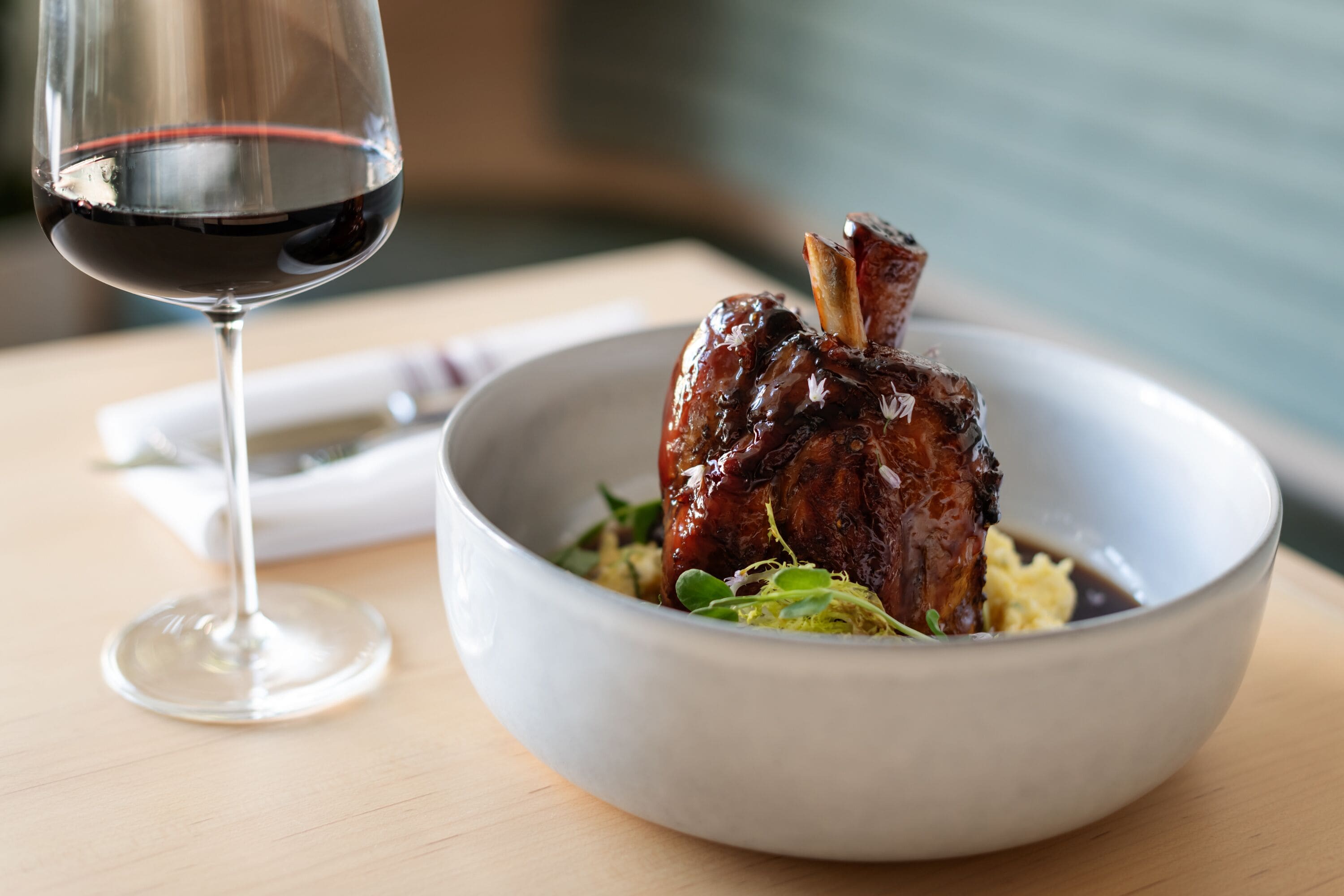 Uma tigela de comida com um copo de vinho tinto sobre uma mesa.