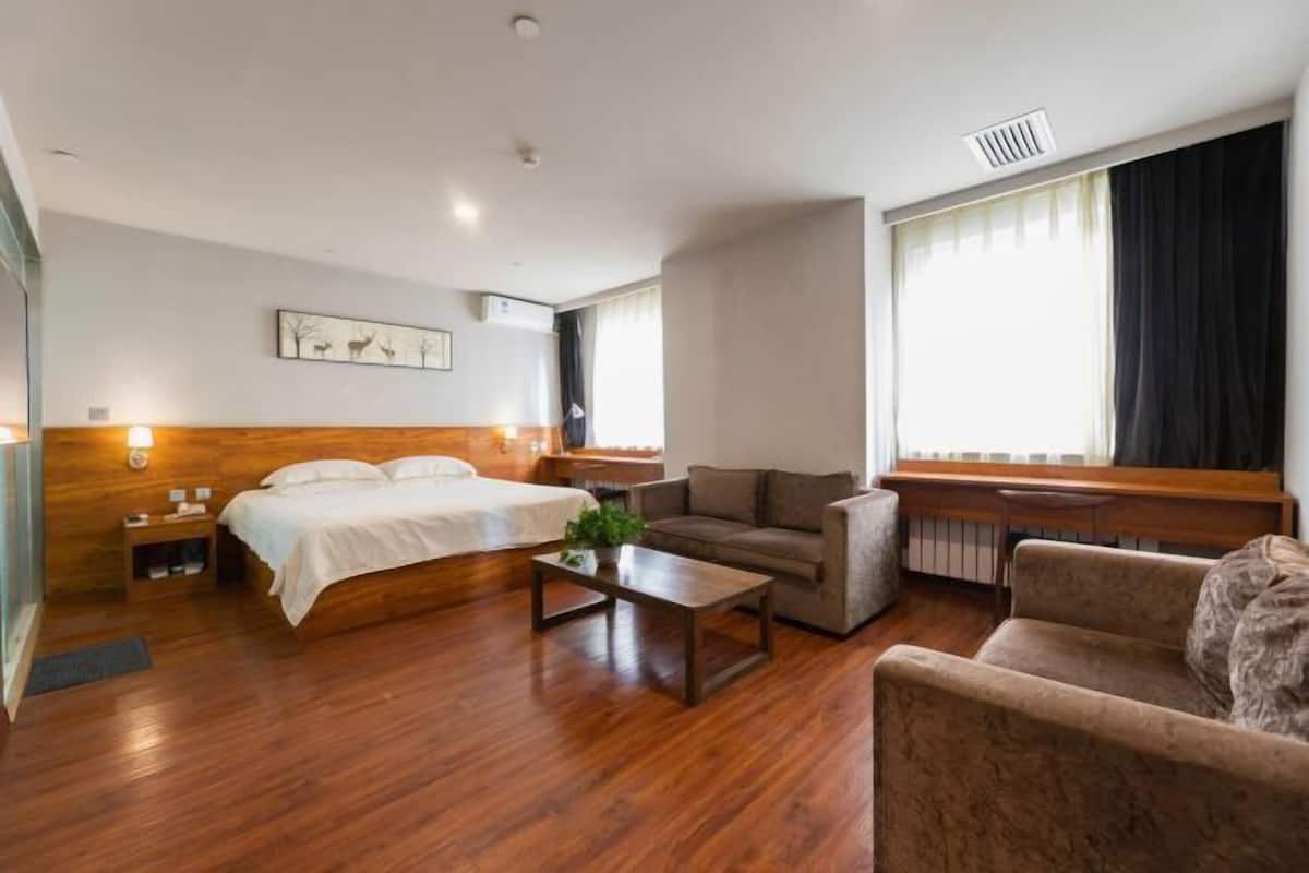 Quarto de hotel com cama, sofá, mesa de centro, janela com cortinas e ar-condicionado fixado na parede.