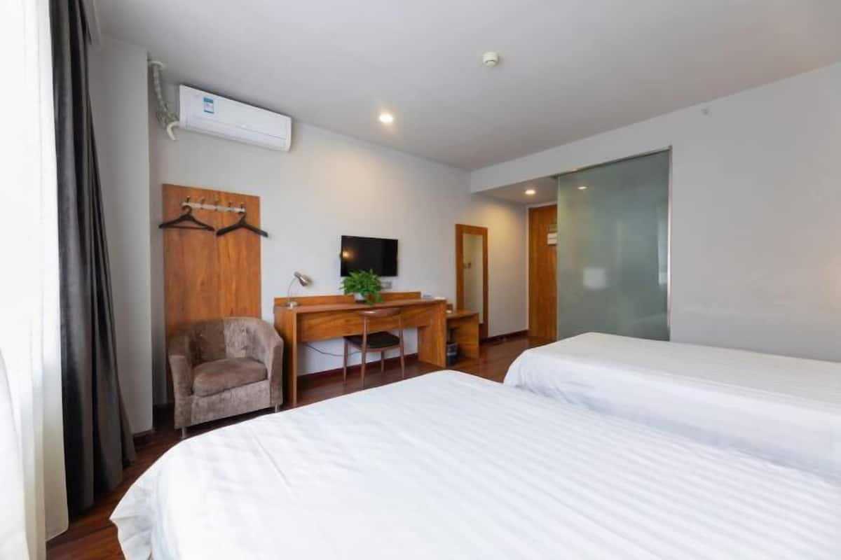 Quarto de hotel com duas camas, uma escrivaninha, uma cadeira, uma televisão e uma porta de correr.