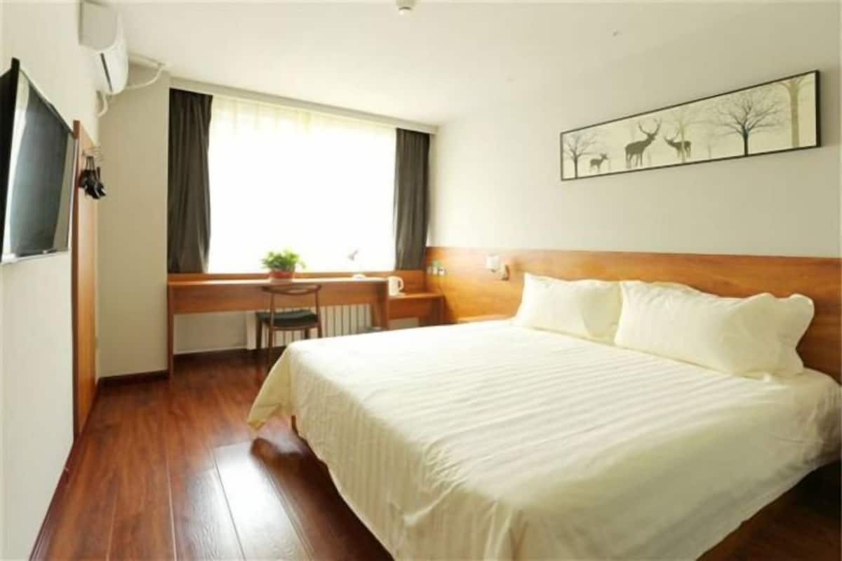 Quarto de hotel com cama, escrivaninha, cadeira, janela com cortinas e um quadro na parede.