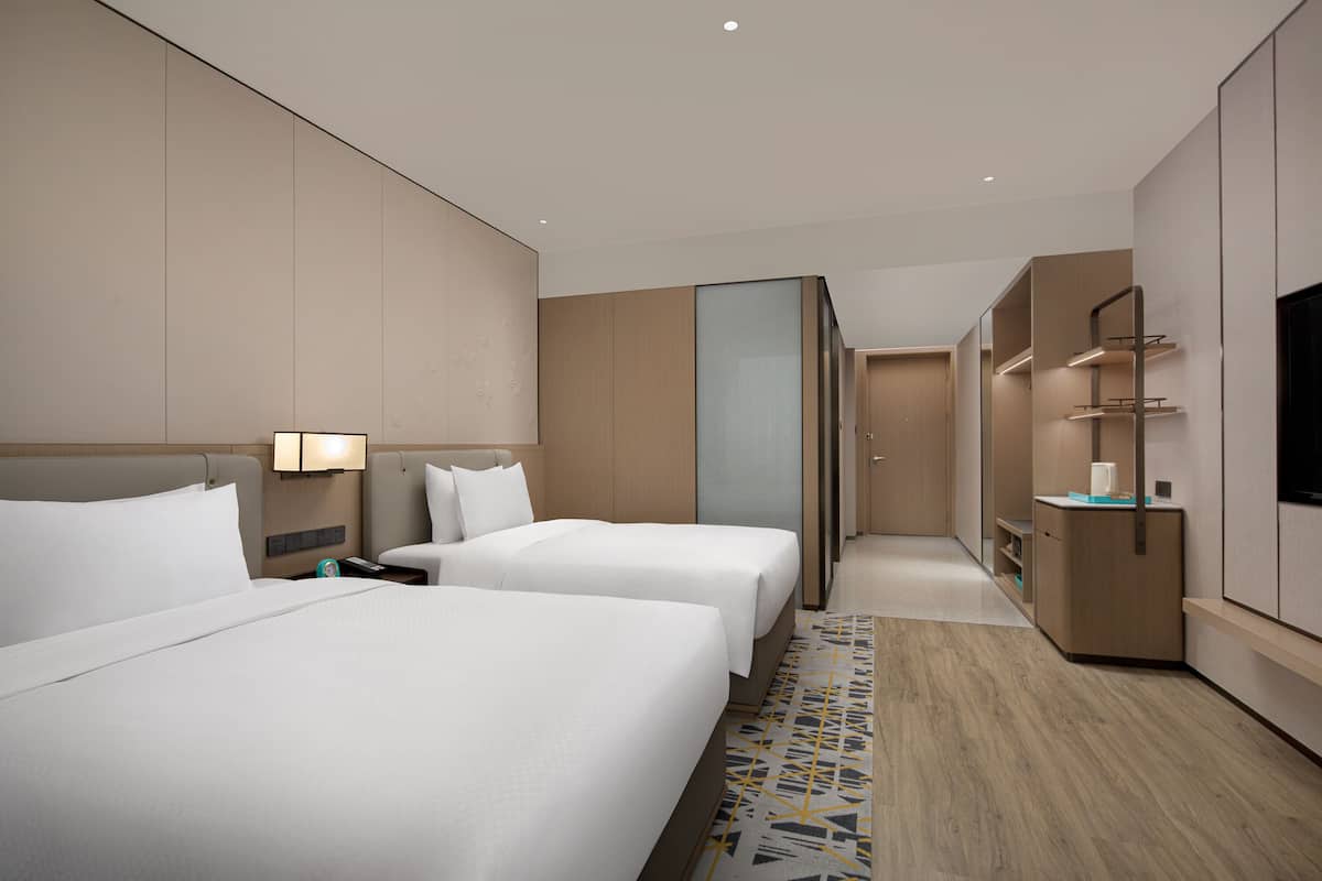 Quarto de hotel com duas camas, televisão, escrivaninha e guarda-roupa.