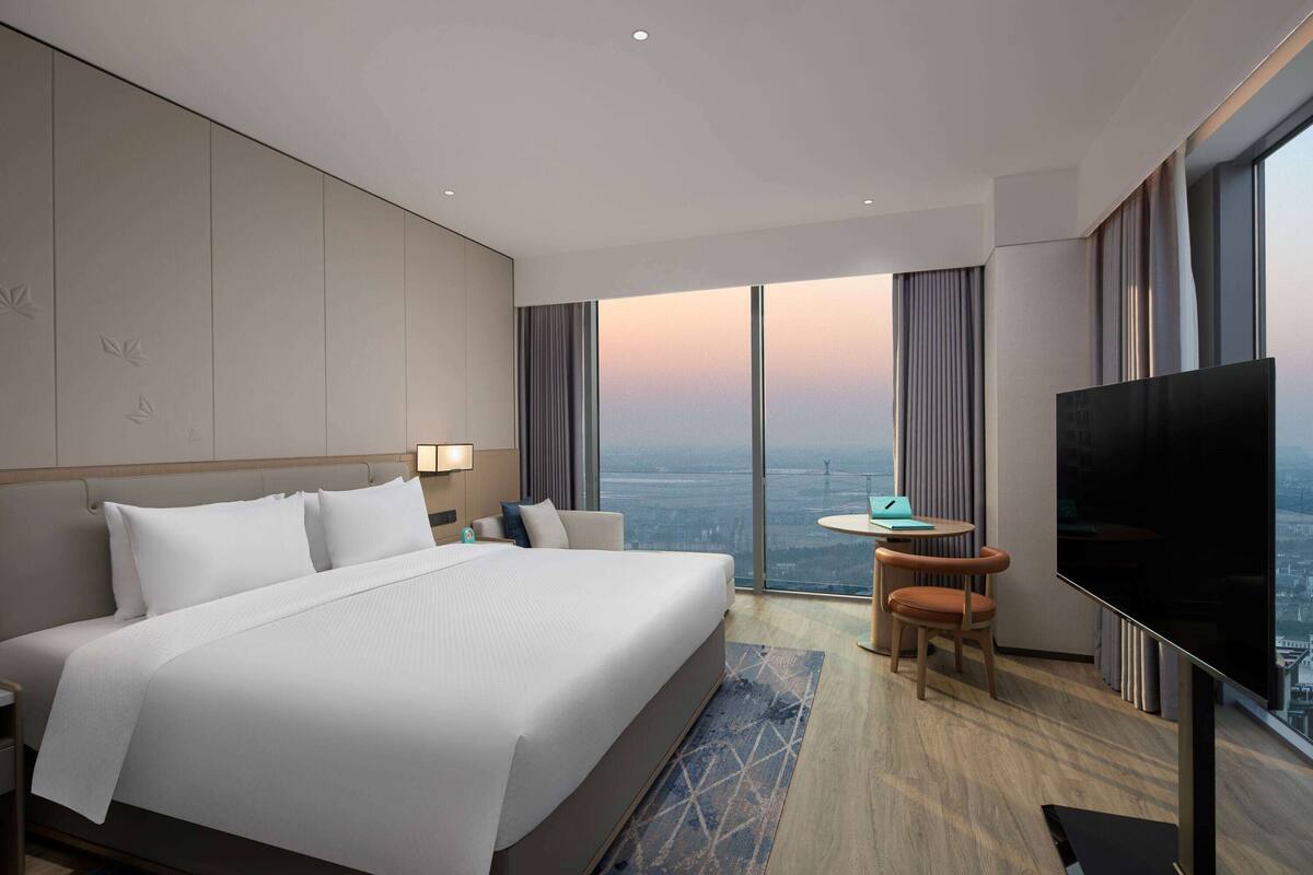 Quarto de hotel moderno com uma cama grande, uma TV, uma mesa pequena e uma cadeira.