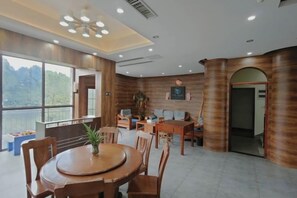 Quarto de hotel com área de refeições, uma grande janela e vista, e um balcão de recepção.