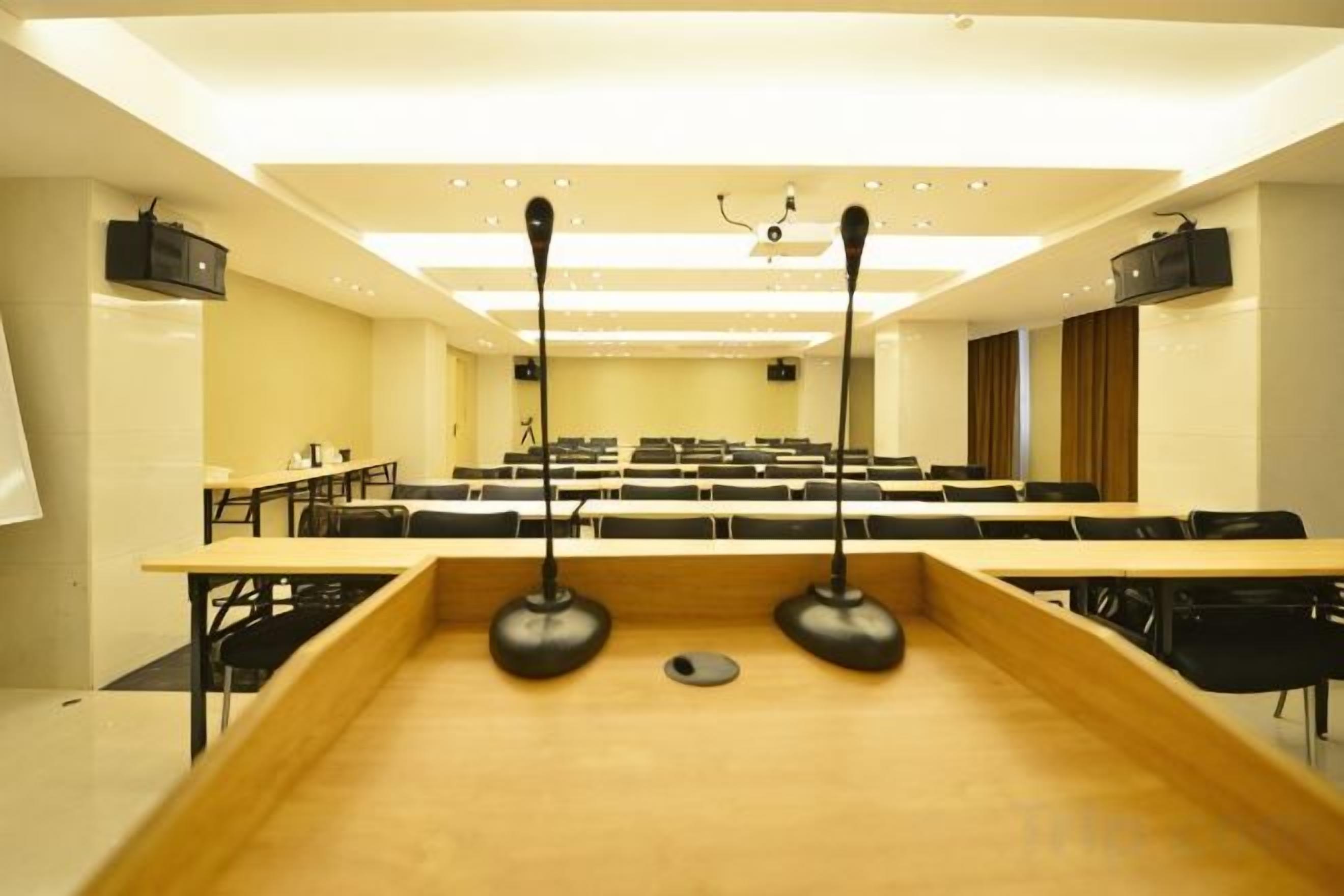 Sala de conferências com mesas e cadeiras dispostas em fileiras, um púlpito e um projetor no teto.
