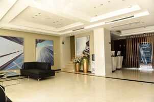 Um lobby moderno com uma mesa de recepção, um sofá preto e uma grande obra de arte na parede.