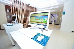 Uma mesa de recepção com monitor de computador exibindo uma interface colorida, um mouse em um apoio e um divisório de madeira ao fundo.