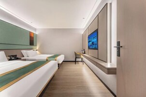 Quarto de hotel com duas camas, televisão, escrivaninha e um espelho grande.