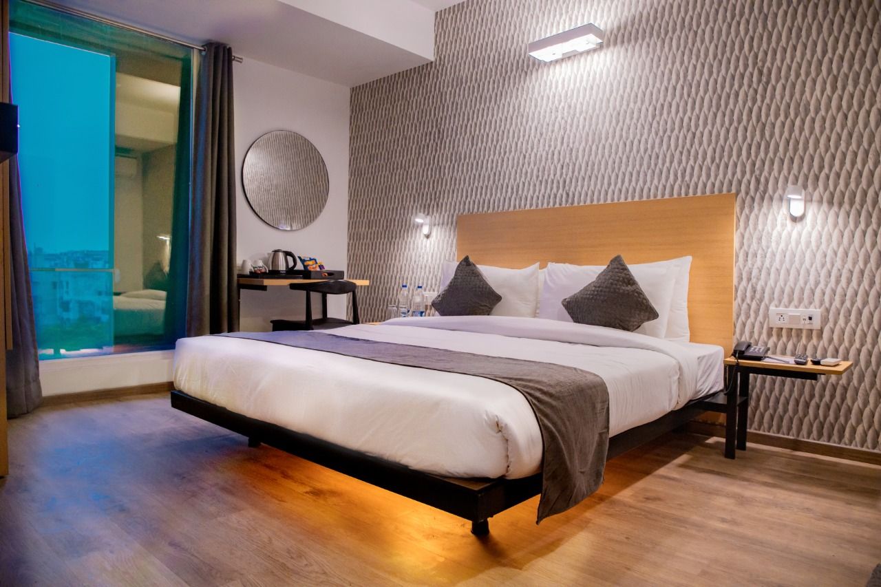 Quarto de hotel moderno com uma cama grande, uma mesinha de cabeceira, um enfeite redondo na parede e vista através de uma porta de vidro.