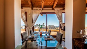 Uma sala de jantar com mesa de vidro, cadeiras e vista para a cidade através de grandes janelas.