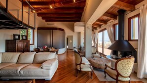 Uma sala de estar ampla com teto alto, vigas de madeira, lareira e vista para a cidade.