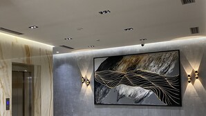 Um elevador moderno com acabamento em mármore, uma grande pintura abstrata na parede e iluminação embutida no teto.