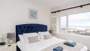 Quarto com uma cama grande, janela com vista, mesa de cabeceira com abajur e obra de arte na parede.