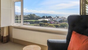 Quarto com uma janela ampla com vista para uma área residencial, um radiador abaixo e uma cadeira com almofada.