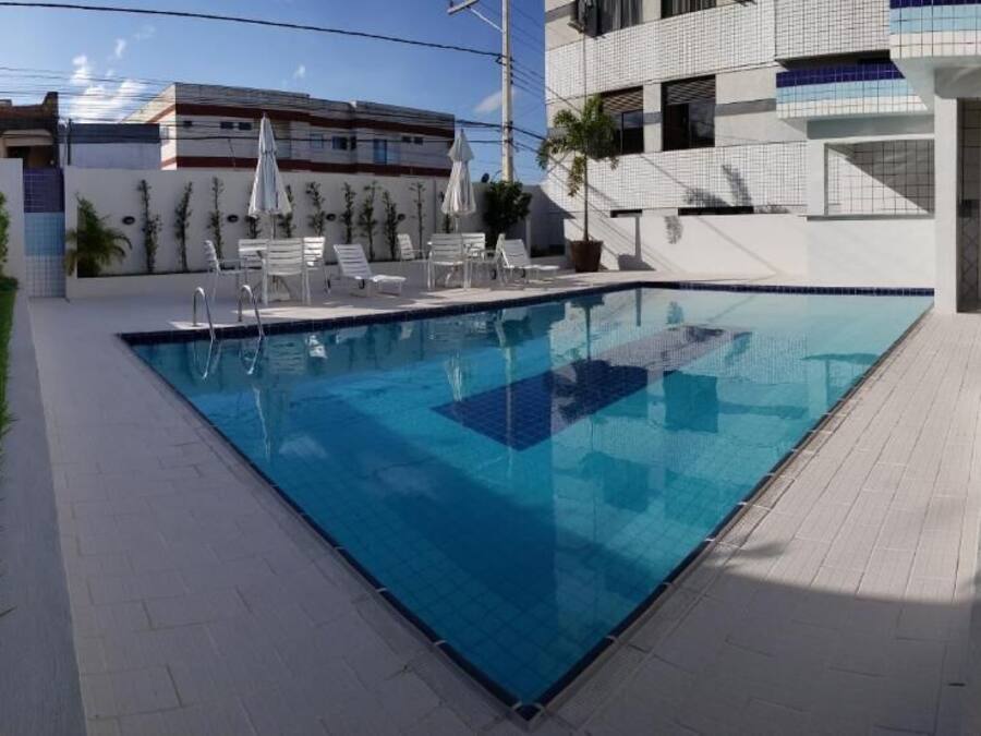 Piscina retangular ao ar livre com um deck revestido, rodeada por espreguiçadeiras e vasos de plantas.