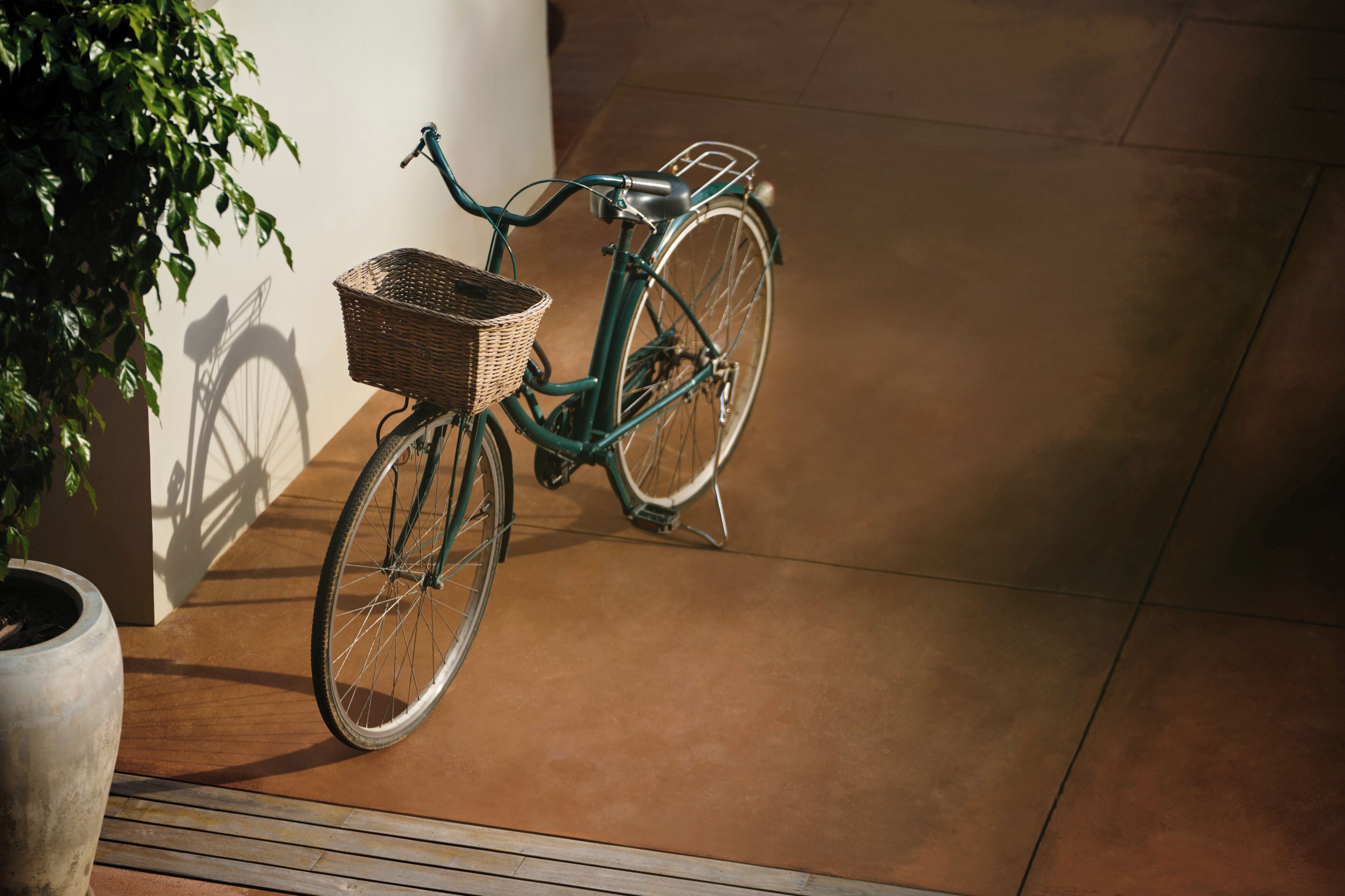Uma bicicleta ergométrica com cesto, colocada sobre piso cerâmico próximo a uma parede.