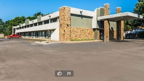 Um edifício moderno com fachada de pedra, área de estacionamento coberta e um carro vermelho estacionado na frente.