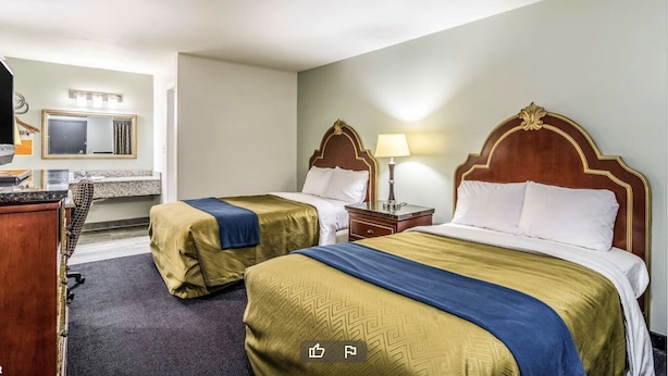 Quarto de hotel com duas camas, uma escrivaninha, uma cadeira, um espelho e um abajur.