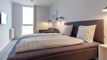 Quarto com cama, mesas de cabeceira, um criado-mudo, janela e luminária na parede.
