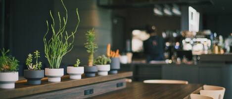 Uma área de bar com balcão de madeira, plantas em vasos e banquetas.
