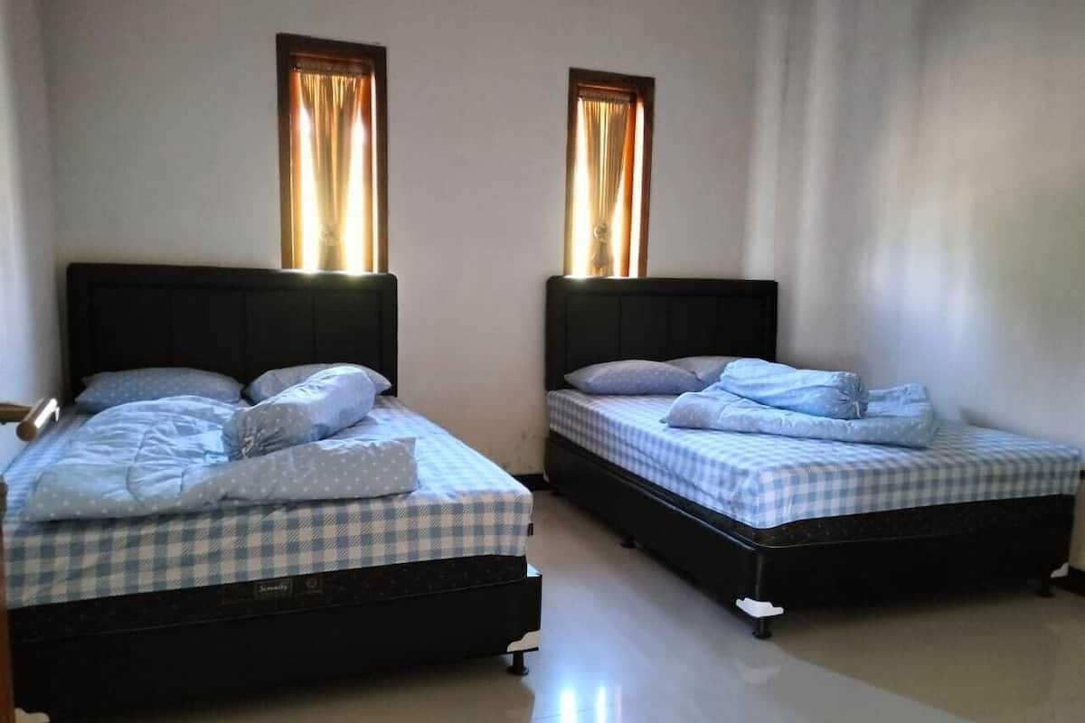 Duas camas de solteiro com cabeceiras, uma parede lisa e uma janela com cortinas.