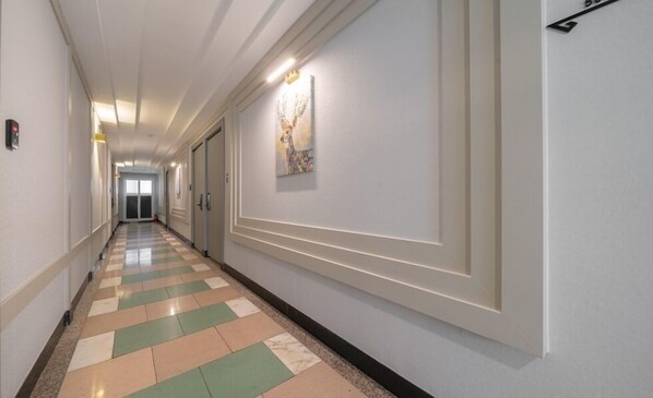 Um corredor comprido e estreito com piso xadrez, paredes brancas e uma obra de arte emoldurada na parede da direita.