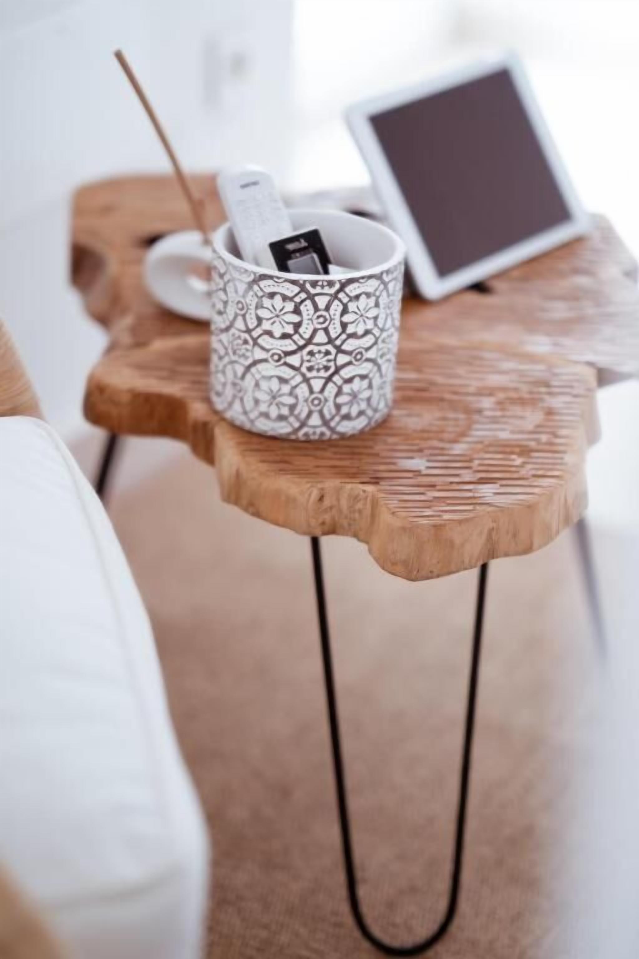 Uma mesa de centro de madeira com uma caneca branca contendo um saquinho de chá e um smartphone. Um tablet está sobre a mesa.