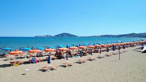 Uma praia com fileiras de espreguiçadeiras e guarda-sóis, céu azul límpido e mar calmo.