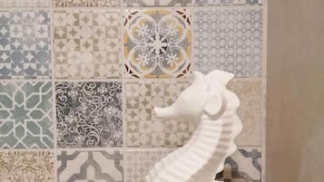 Casa de banho com parede revestida de azulejos com padrões geométricos e florais diversos. Uma escultura de cavalo-marinho branco está colocada no chão.