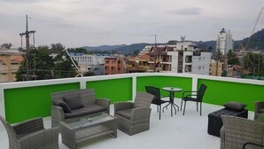 Terraço no telhado com móveis de vime, uma mesa de vidro e vista para a paisagem urbana.