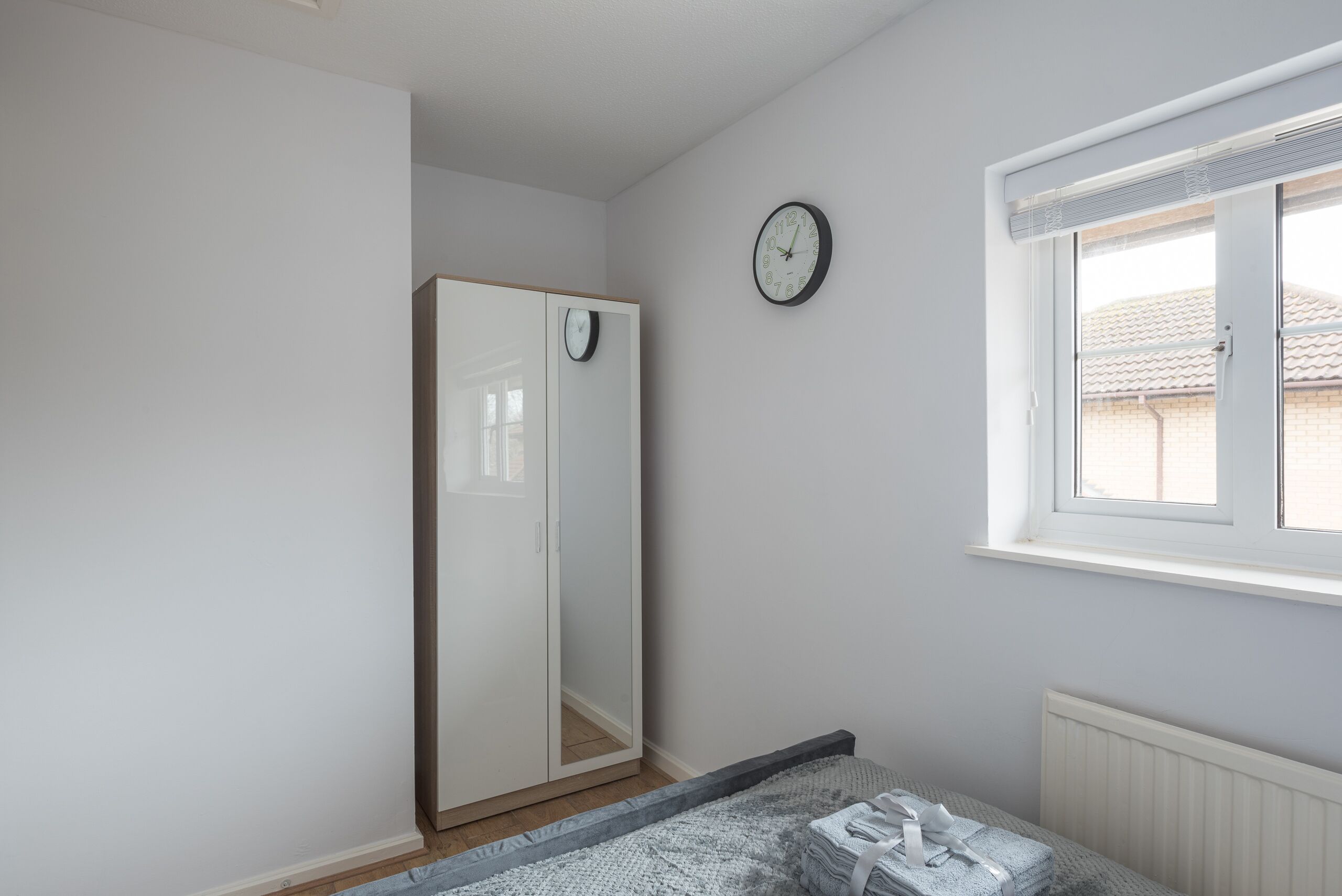 Quarto com guarda-roupa espaçoso, relógio na parede e janela com vista para um edifício.