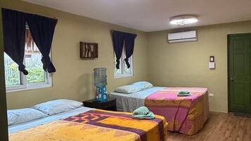 Quarto com duas camas, bebedouro, ventilador de teto e porta verde.
