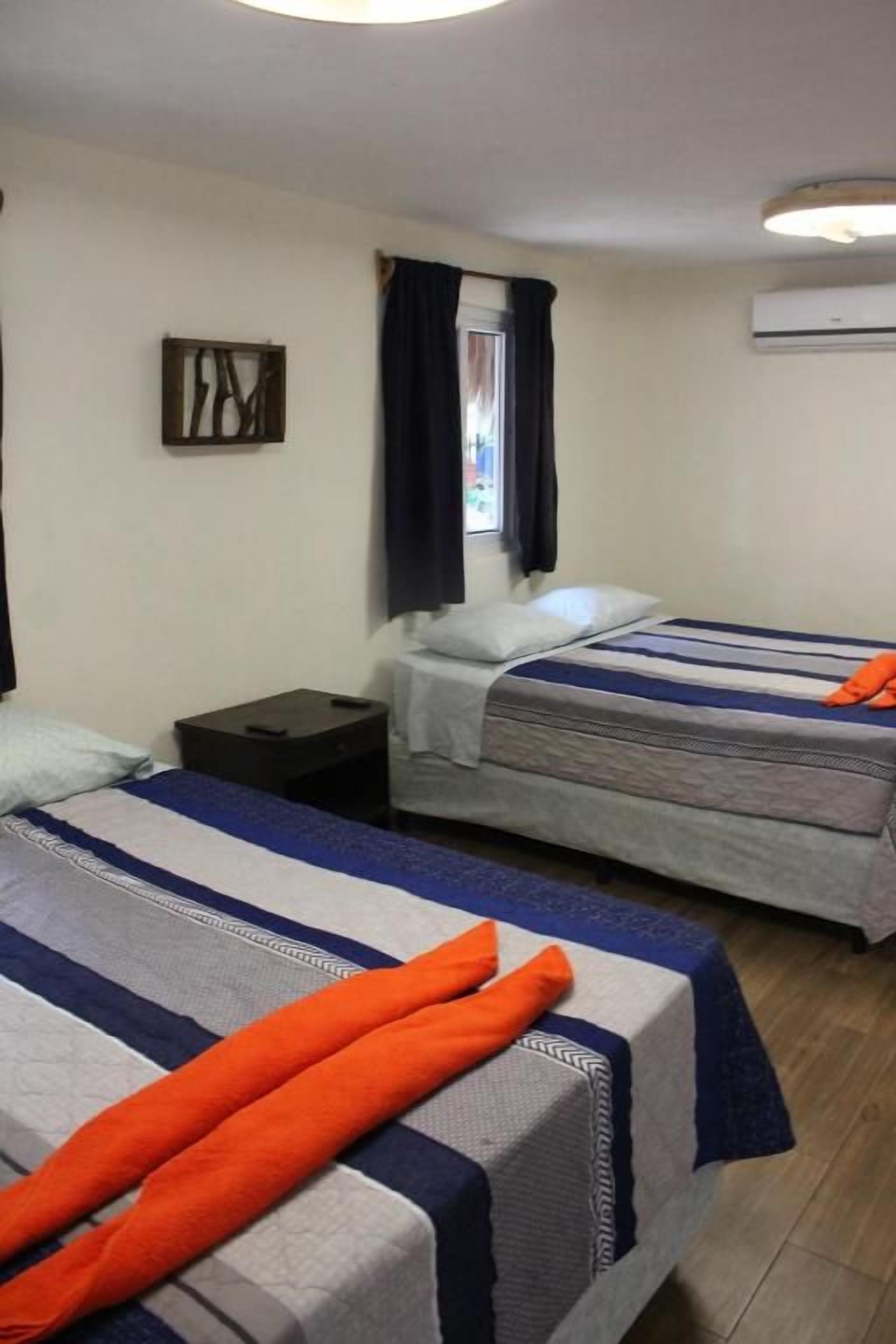 Quarto de hotel com duas camas, mesa de cabeceira, janela com cortinas e aparelho de ar condicionado.