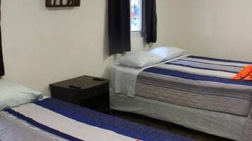 Quarto de hotel com duas camas, mesa de cabeceira, janela com cortinas e aparelho de ar condicionado.