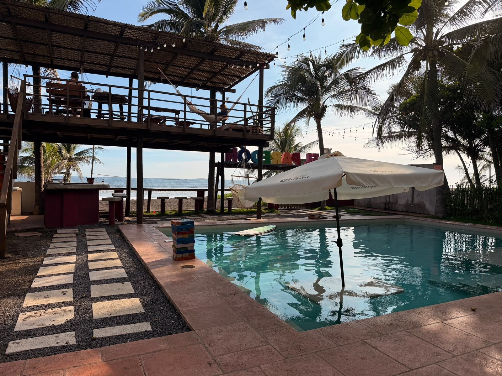 Uma área de piscina com deck de madeira, uma espreguiçadeira e vista para o mar.