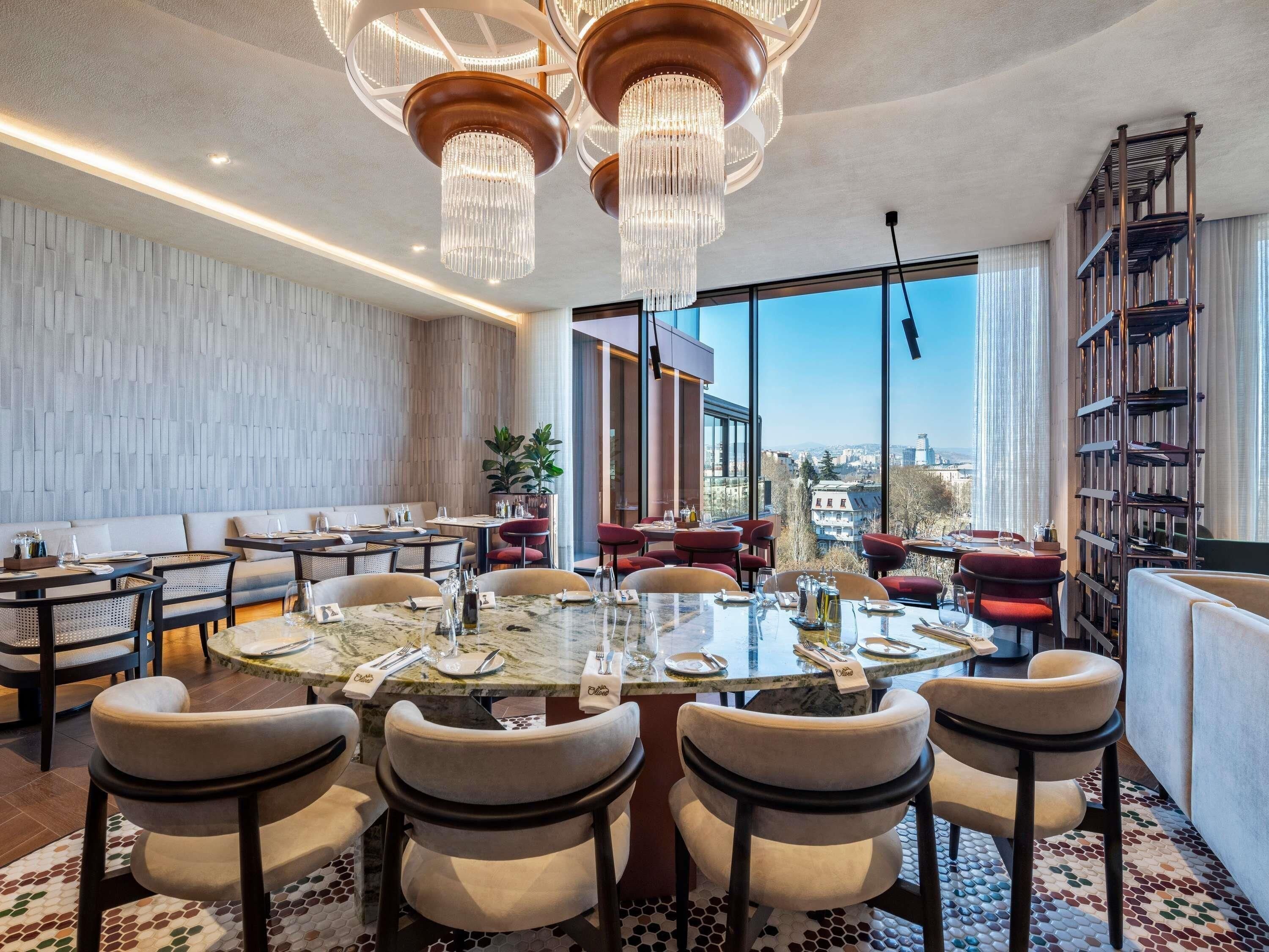 Uma área de jantar moderna com uma mesa redonda, várias cadeiras e um candelabro.