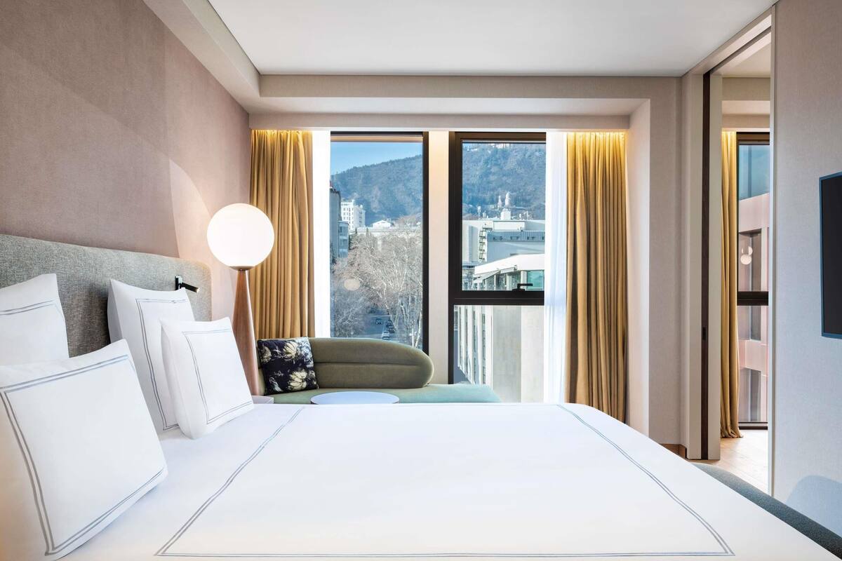 Quarto de hotel com uma cama grande, vista para o horizonte urbano e design moderno.