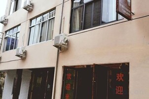 Fachada de edifício com várias janelas, algumas com aparelhos de ar condicionado, e uma placa com caracteres chineses.