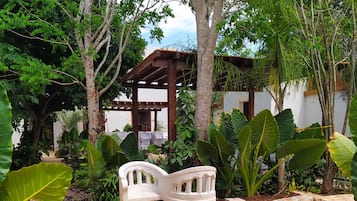 Um jardim com um banco de pedra, rodeado por plantas e árvores grandes e verdes.