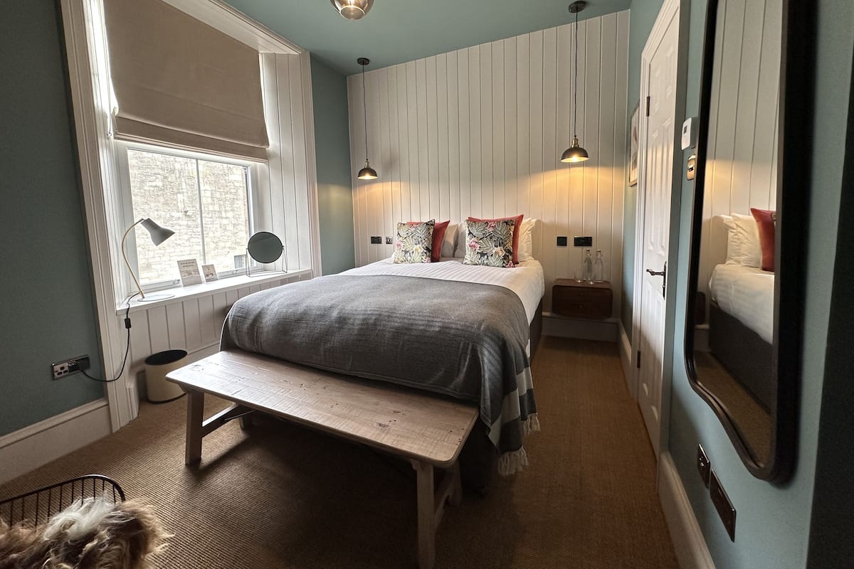 Quarto com cama grande, mesas de cabeceira, um banco, janela e espelho.