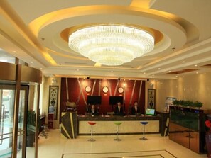 Área de recepção de hotel com um grande candelabro, balcão de recepção e uma área de estar com bancos.
