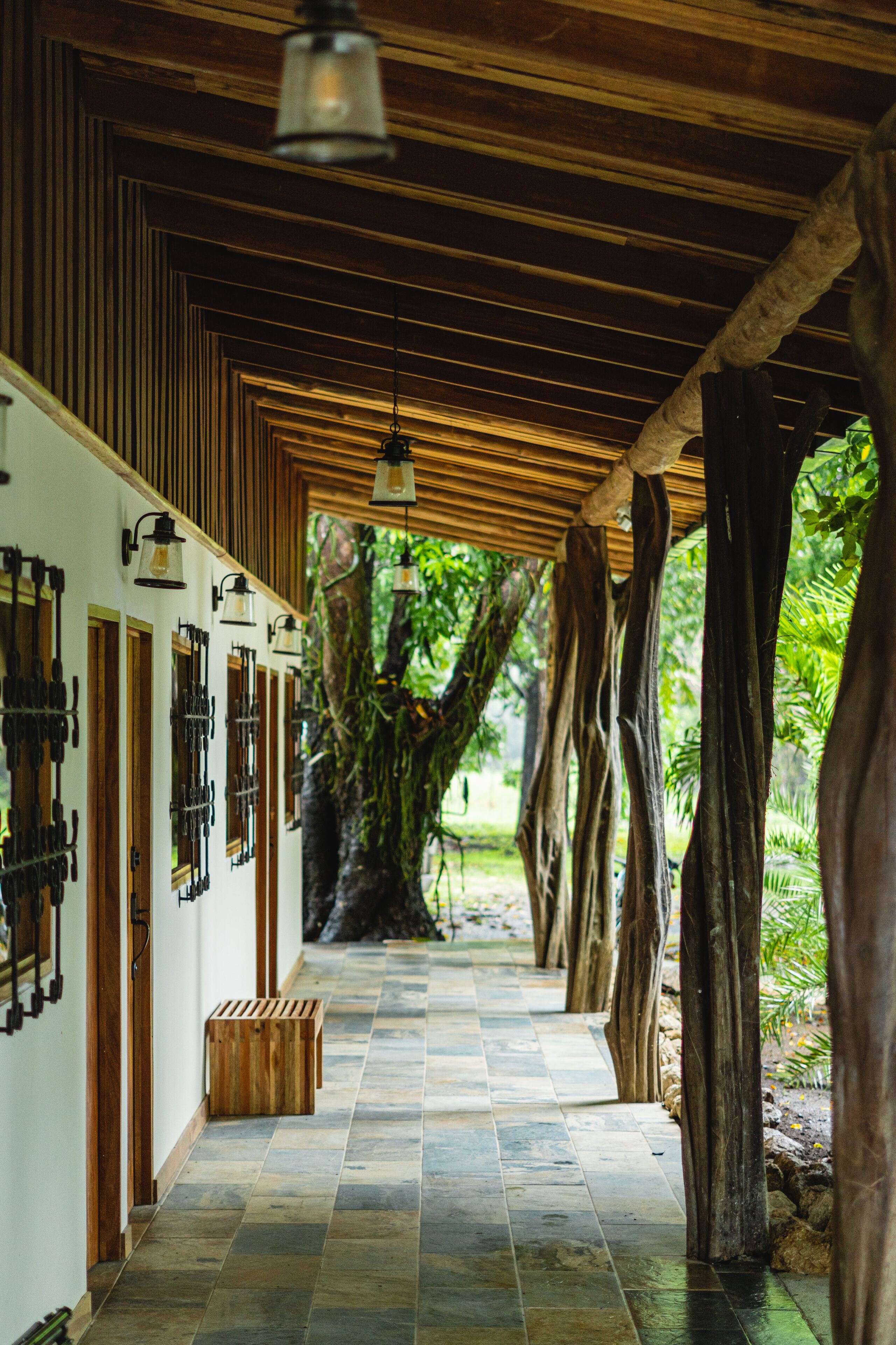 Um corredor com vigas de madeira, pisos de pedra e lanternas penduradas.