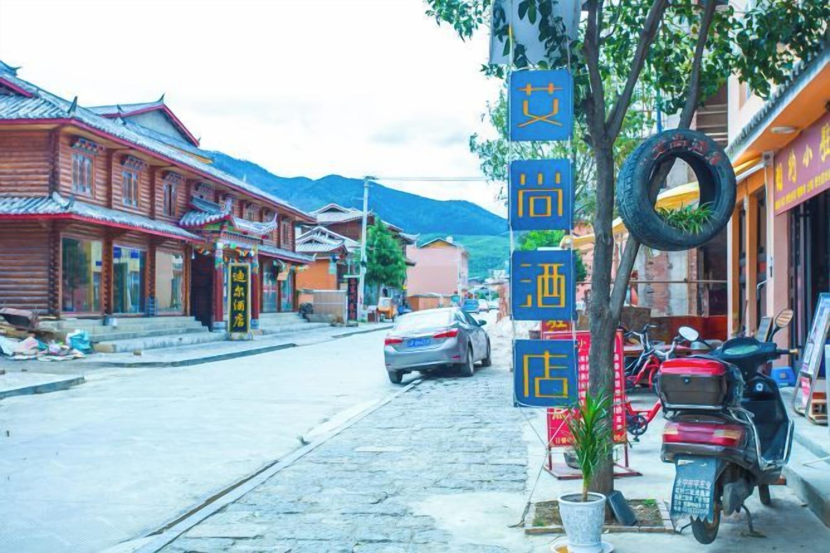 Ruas com edifícios tradicionais, uma árvore com balanço de pneu e motocicletas estacionadas.