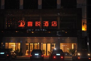 Um hotel com uma placa visível, entrada bem iluminada e área de estacionamento à frente.