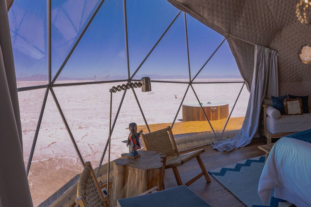 Um quarto acolhedor com uma cama, uma mesinha e uma cadeira, oferecendo vista para uma paisagem extensa através de uma janela ampla.