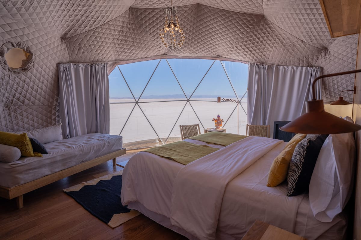 Alojamento em tenda com duas camas, um candelabro e vista para uma paisagem extensa.