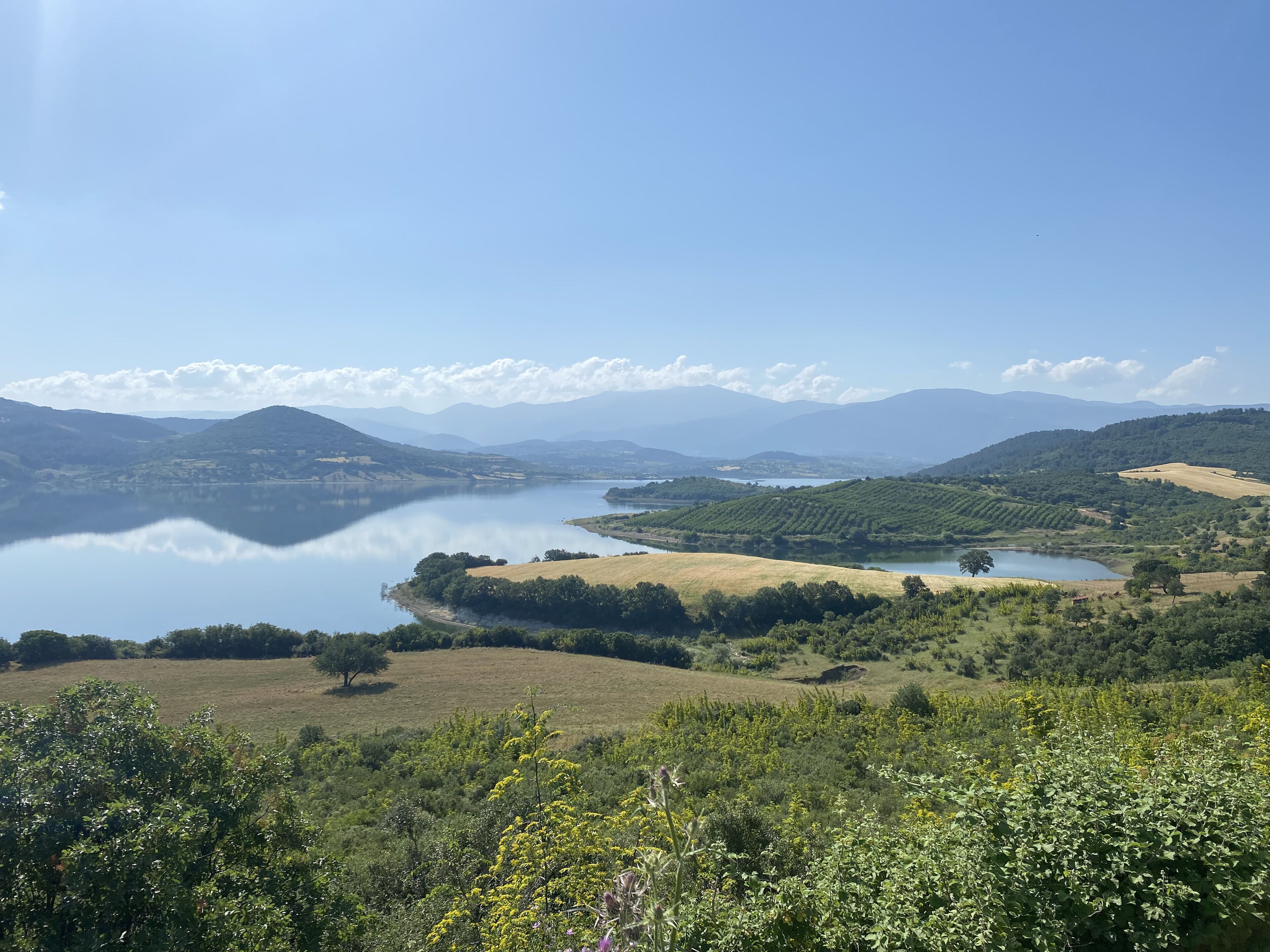 Vista panorâmica de um lago rodeado por colinas e campos.