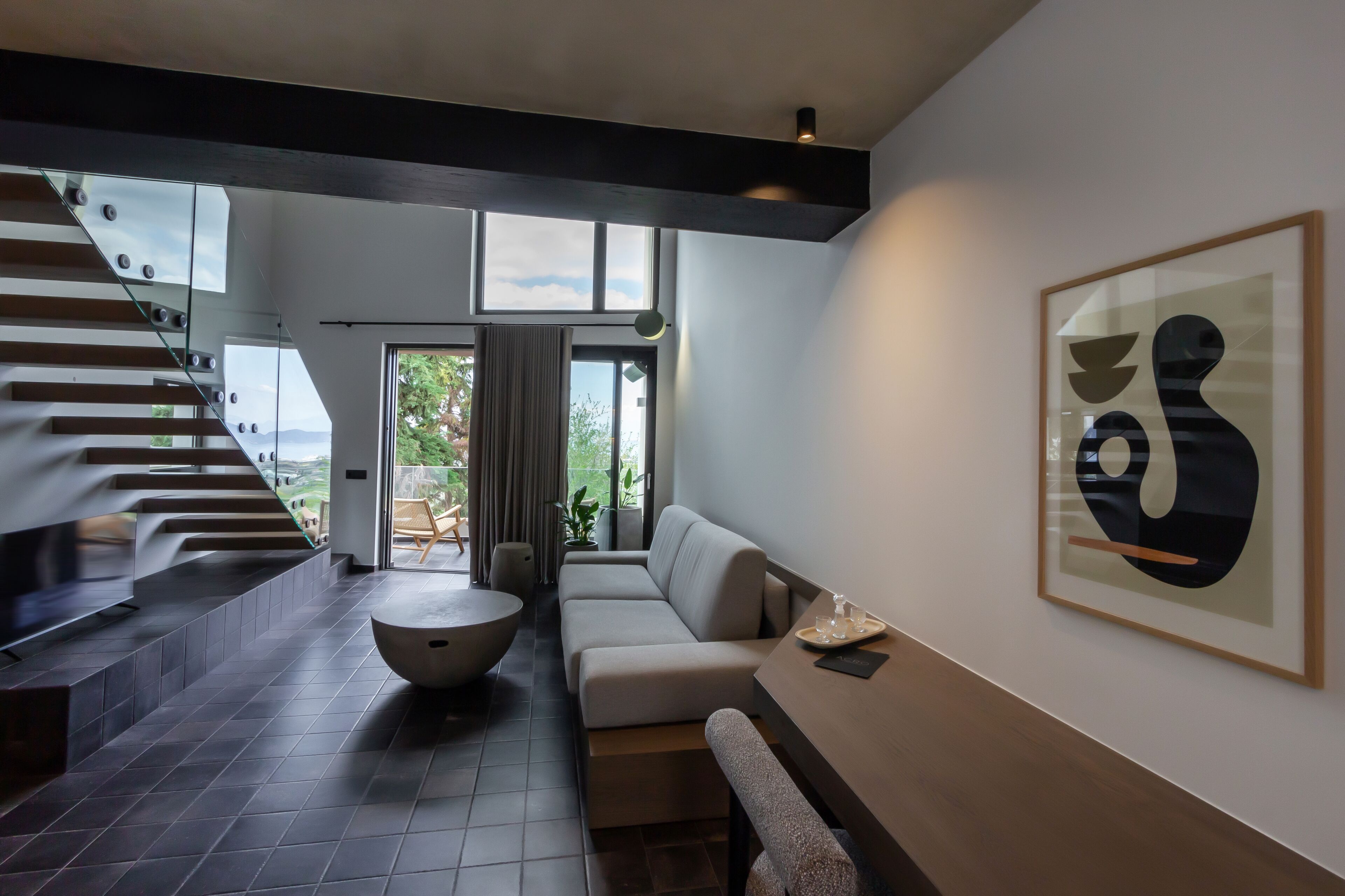 Um interior moderno com escada, sofá, mesa de jantar e uma grande pintura abstrata.