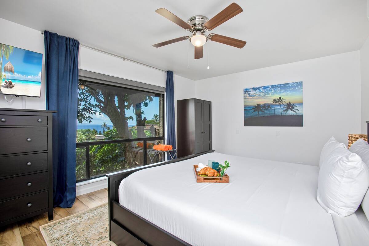Quarto com cama grande, ventoinha no teto, TV, guarda-roupa e varanda com vista para o mar.