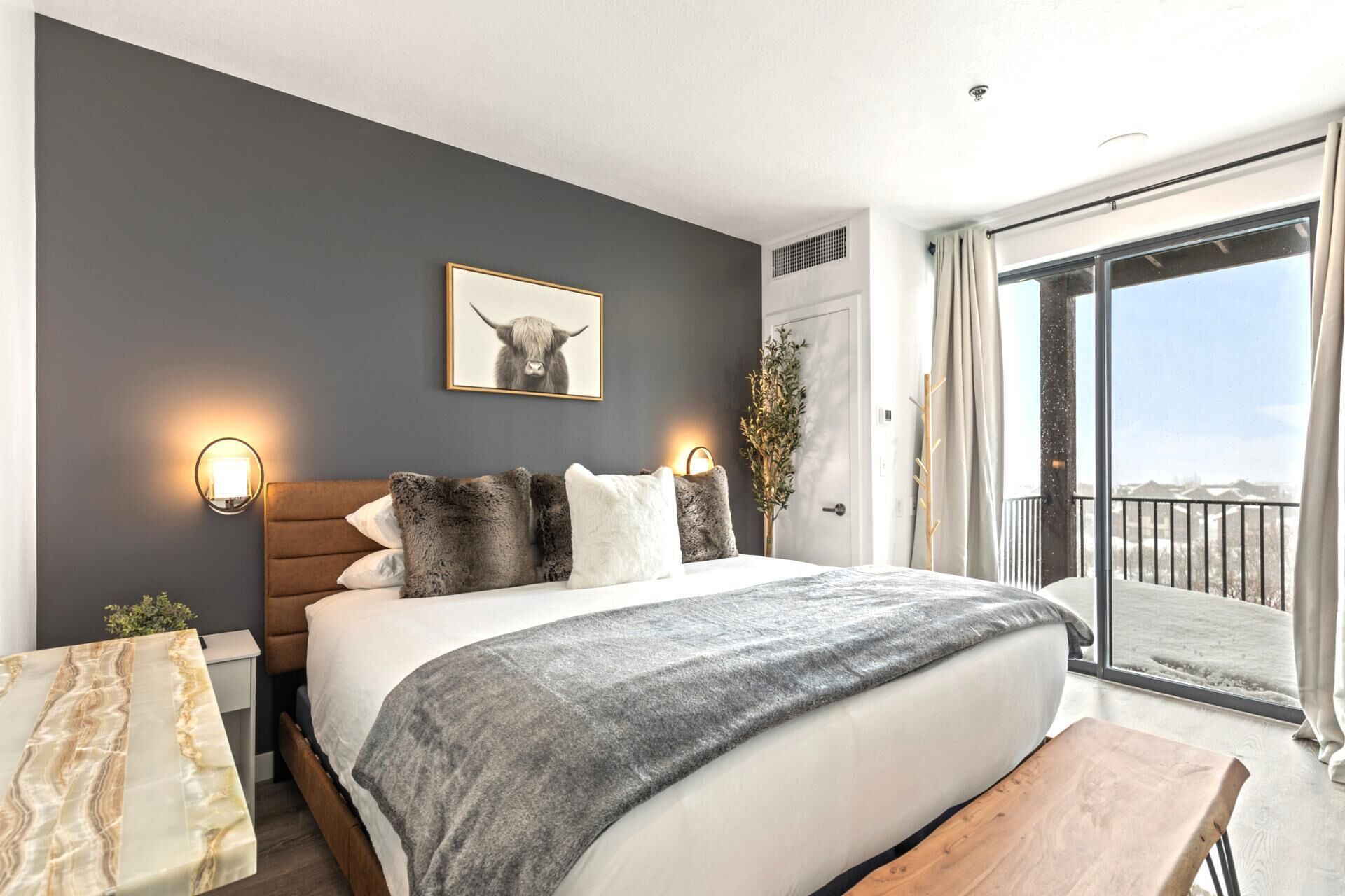 Quarto moderno com cama grande, mesa de cabeceira, mesa de mármore e varanda com vista.