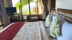 Quarto com cama, televisão, janela vista para o verde e uma pequena mesa.